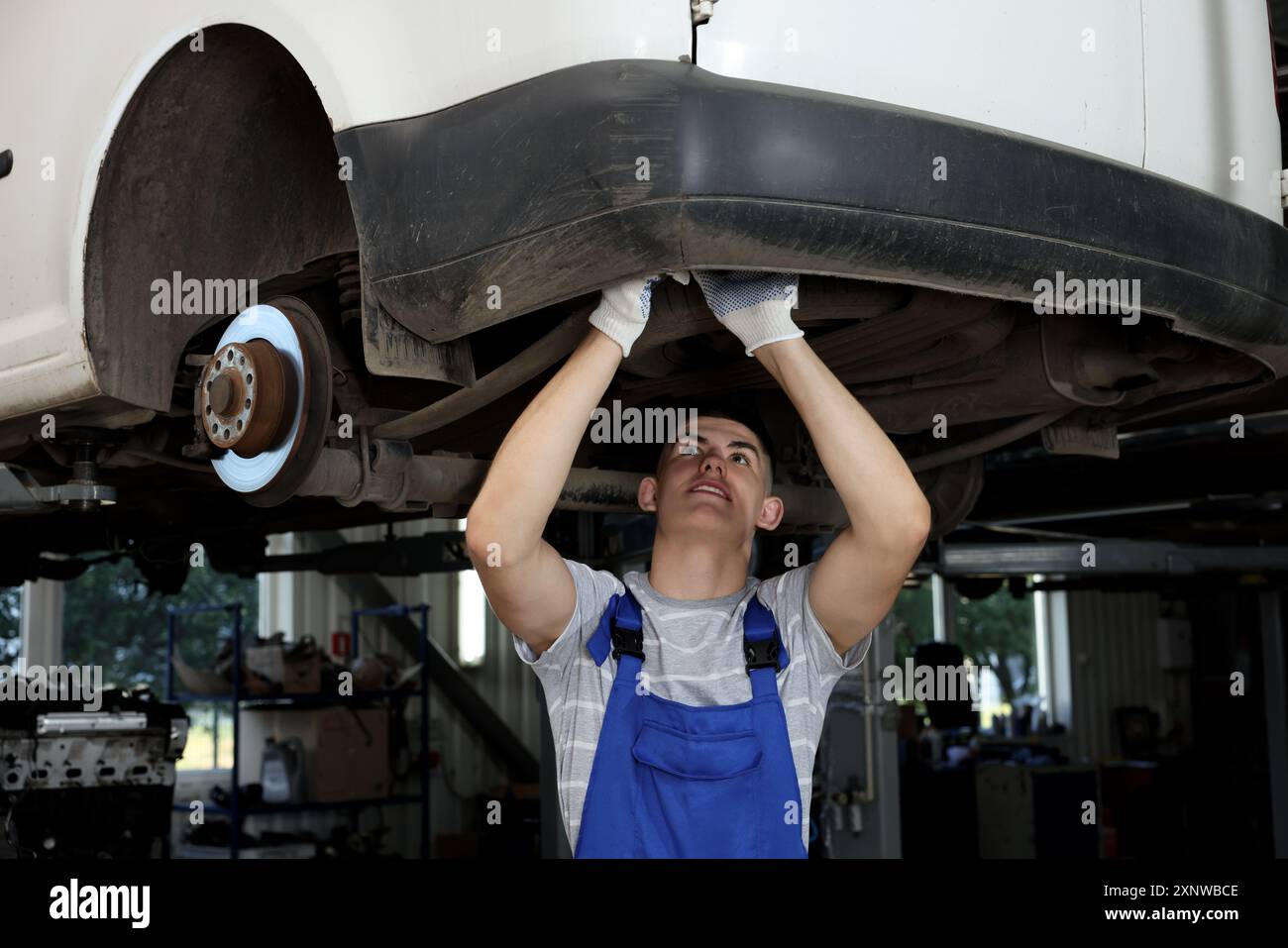 Young auto mechanic fixing lifted car at automobile repair shop Stock ...