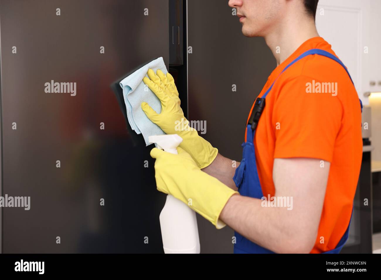 Professional janitor wearing uniform cleaning fridge in kitchen ...
