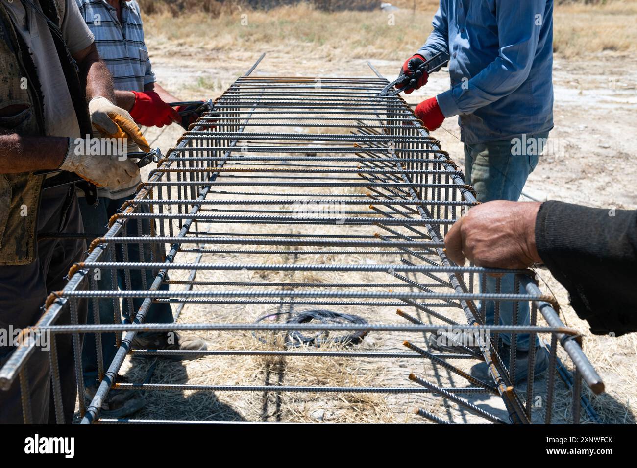 Workers use steel lacing wire to attach steel bars to reinforcing bars ...