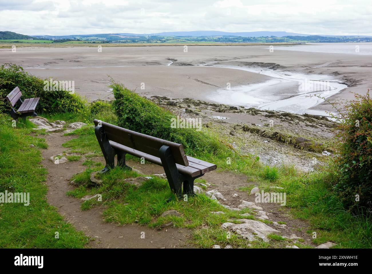 Empty benches overlooking a vast, serene tidal flat with distant hills ...