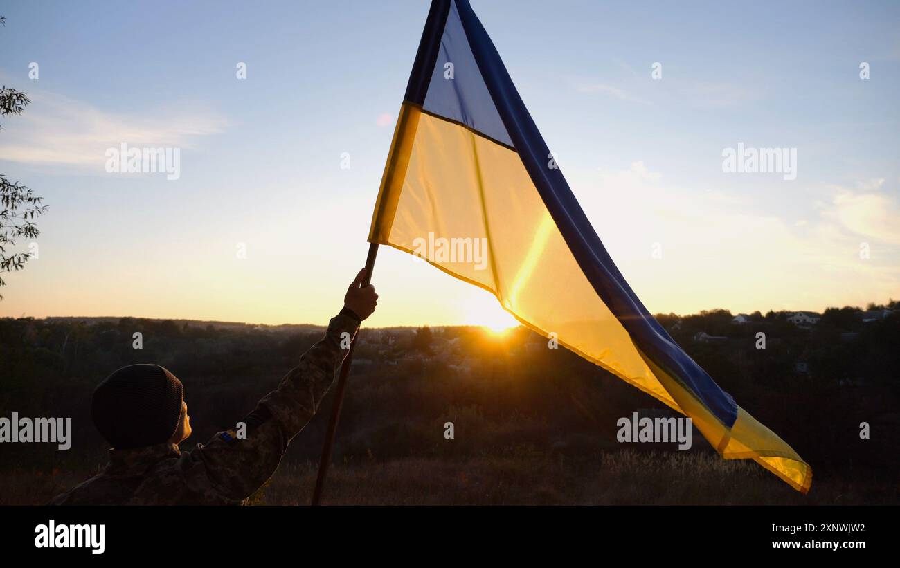 Male soldier stands with raised flag of Ukraine against background of ...