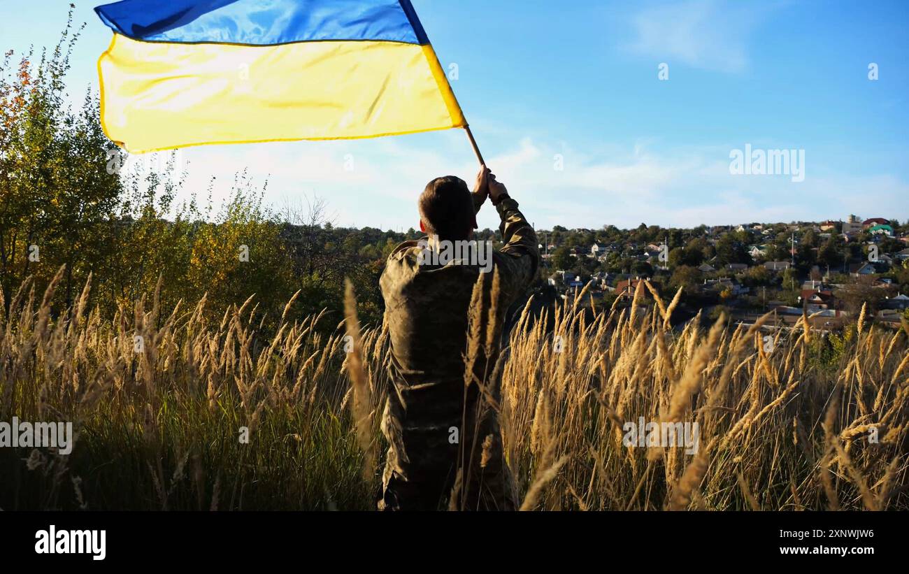 Male military in uniform waving flag of Ukraine at countryside. Young ...