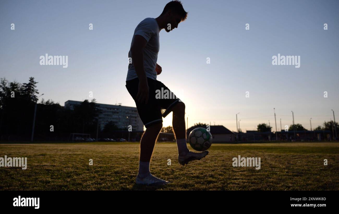 Professional footballer juggling soccer ball on stadium at sunset ...
