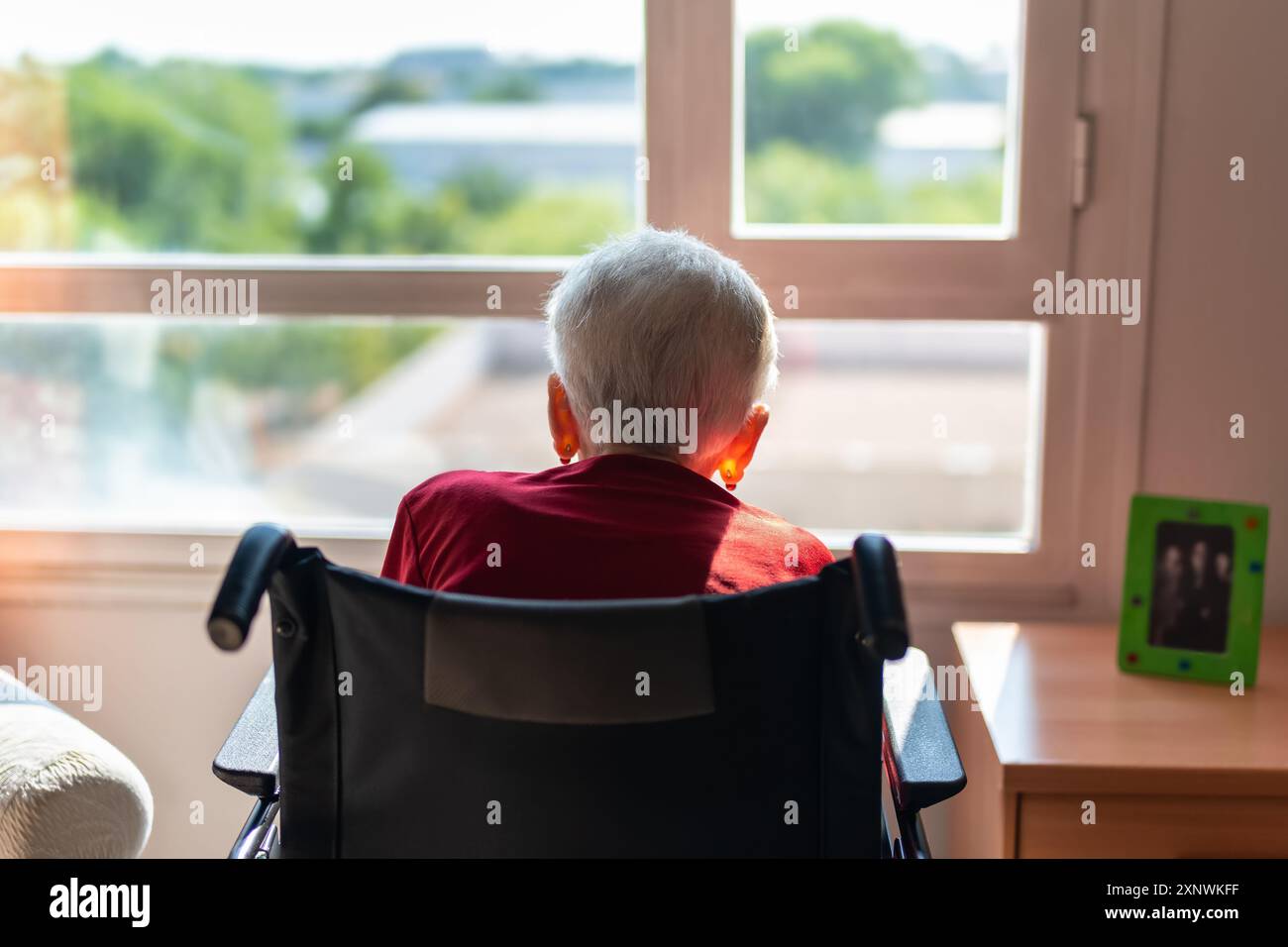 Old woman in wheelchair with her back turned and looking outside ...