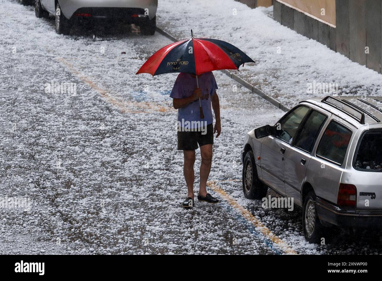 A person holding an umbrella checks the damage to a car after a hail ...