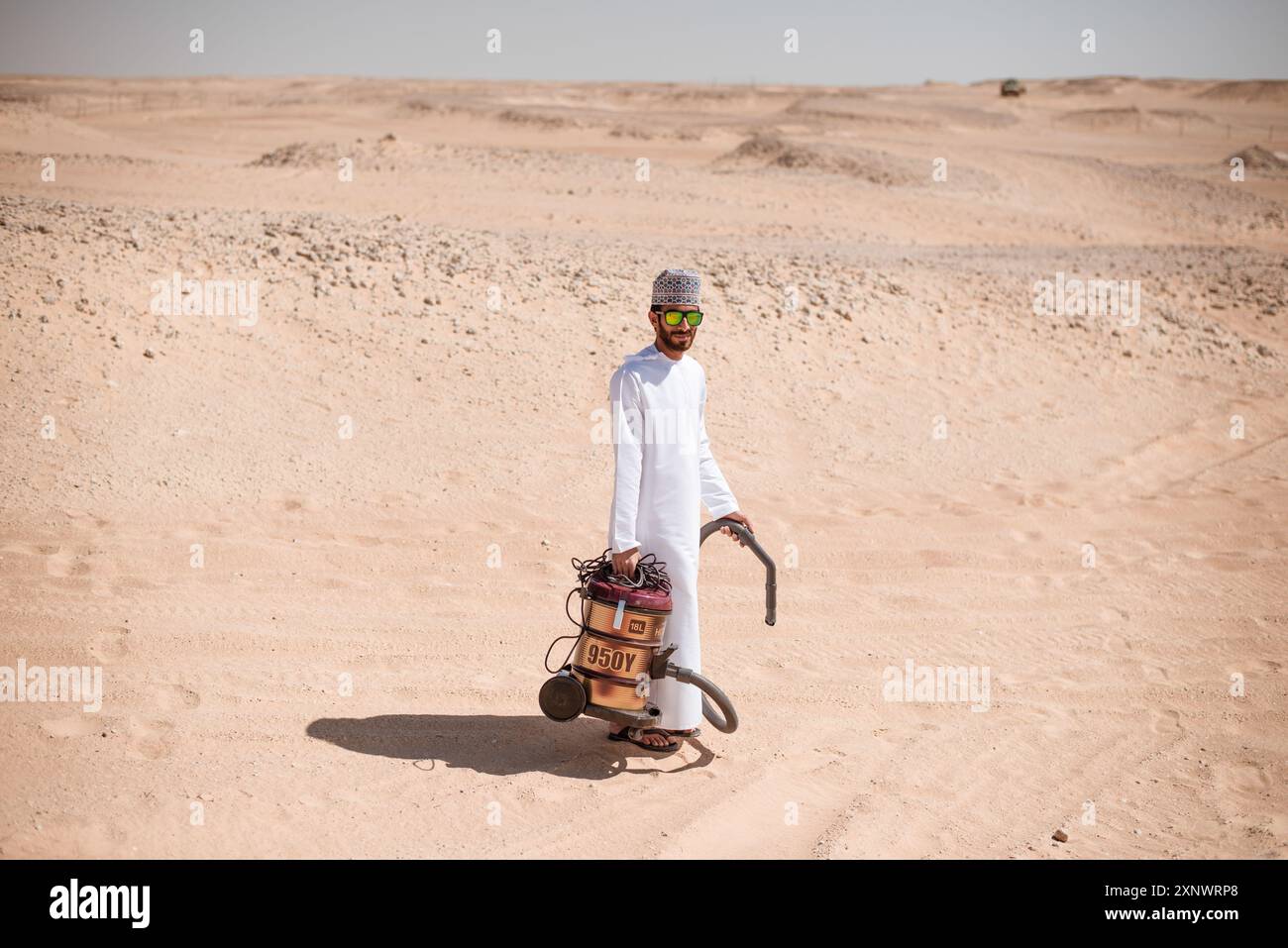 Man in traditional attire holding a vacuum cleaner in a desert ...