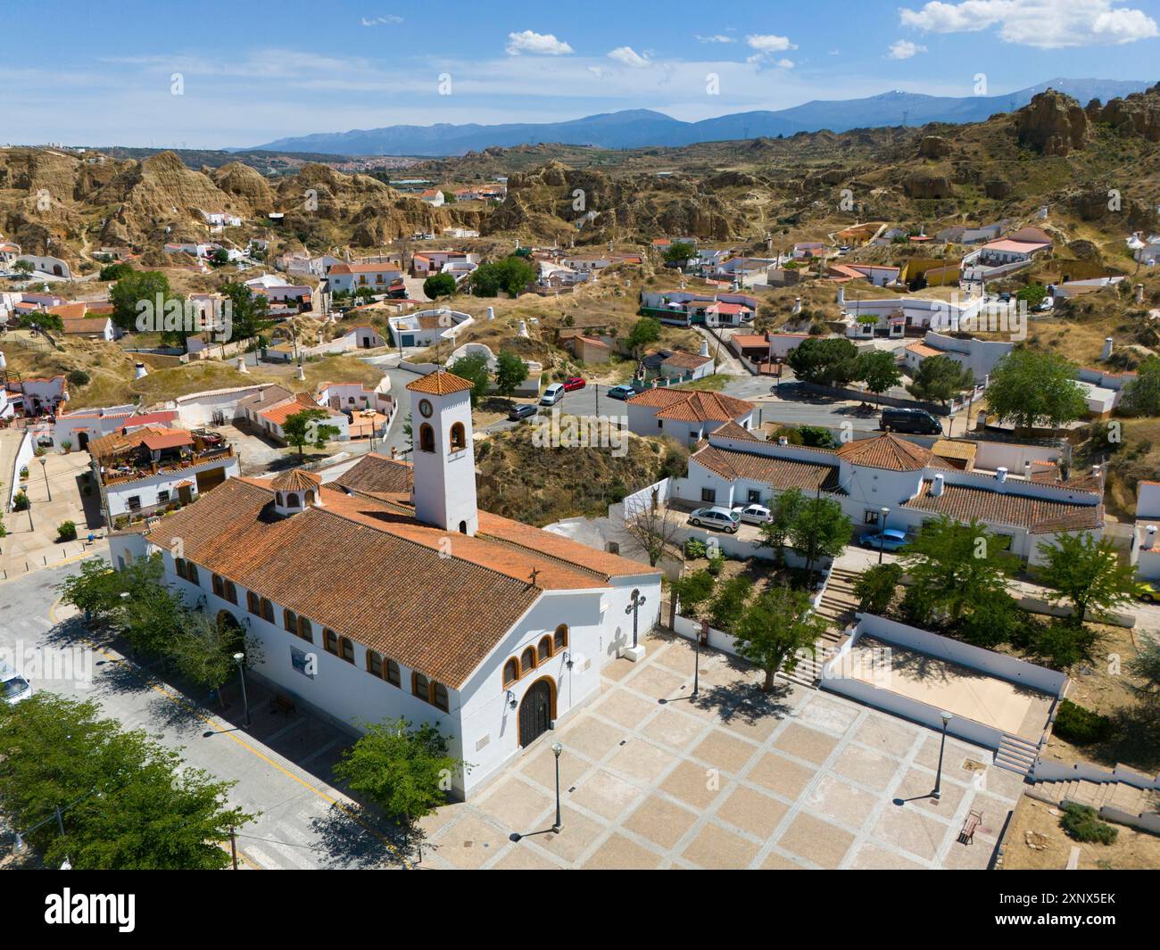 A village square with a church, houses and trees, surrounded by hills ...