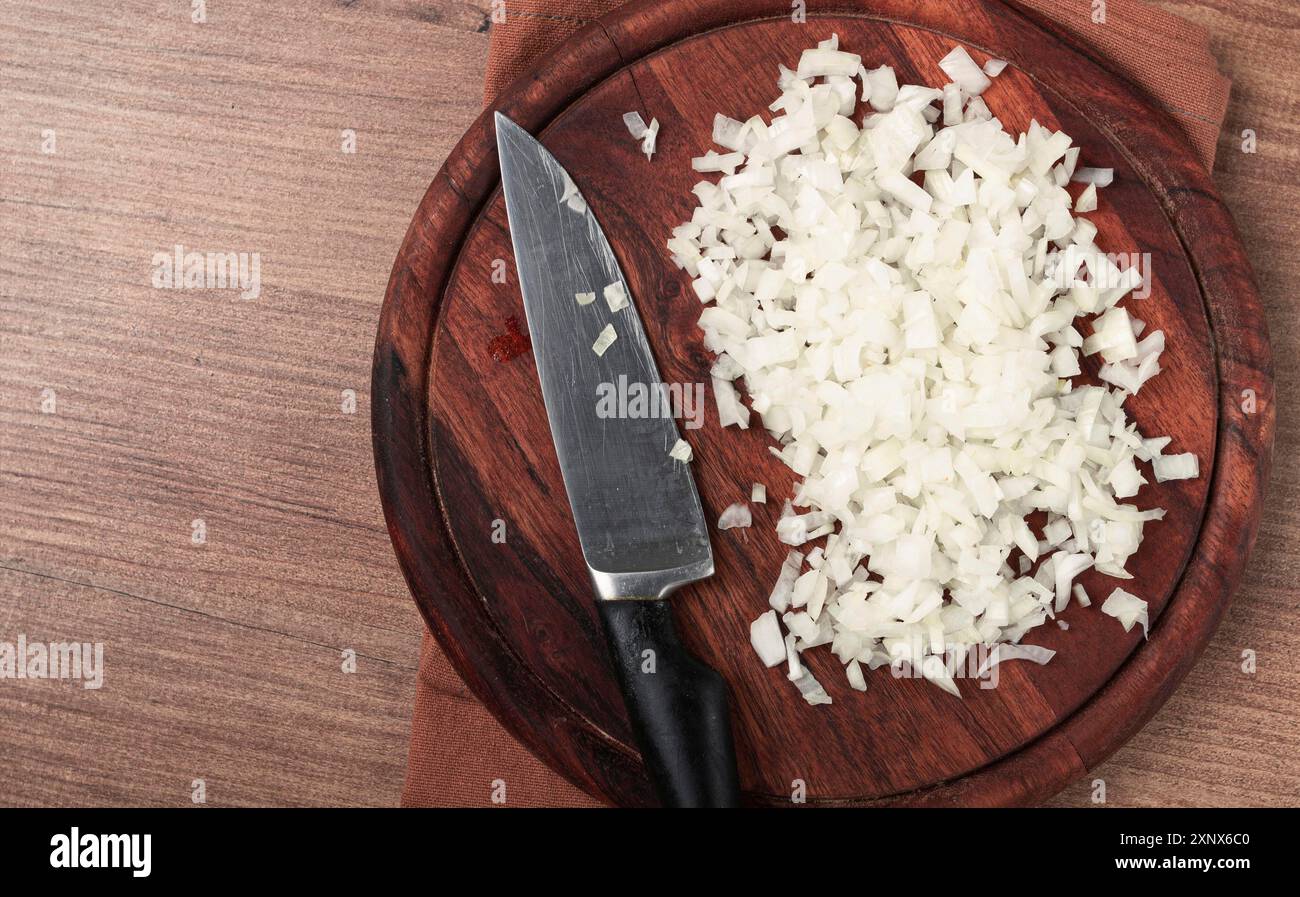 Finely chopped onion on a chopping board with a knife, wooden table ...