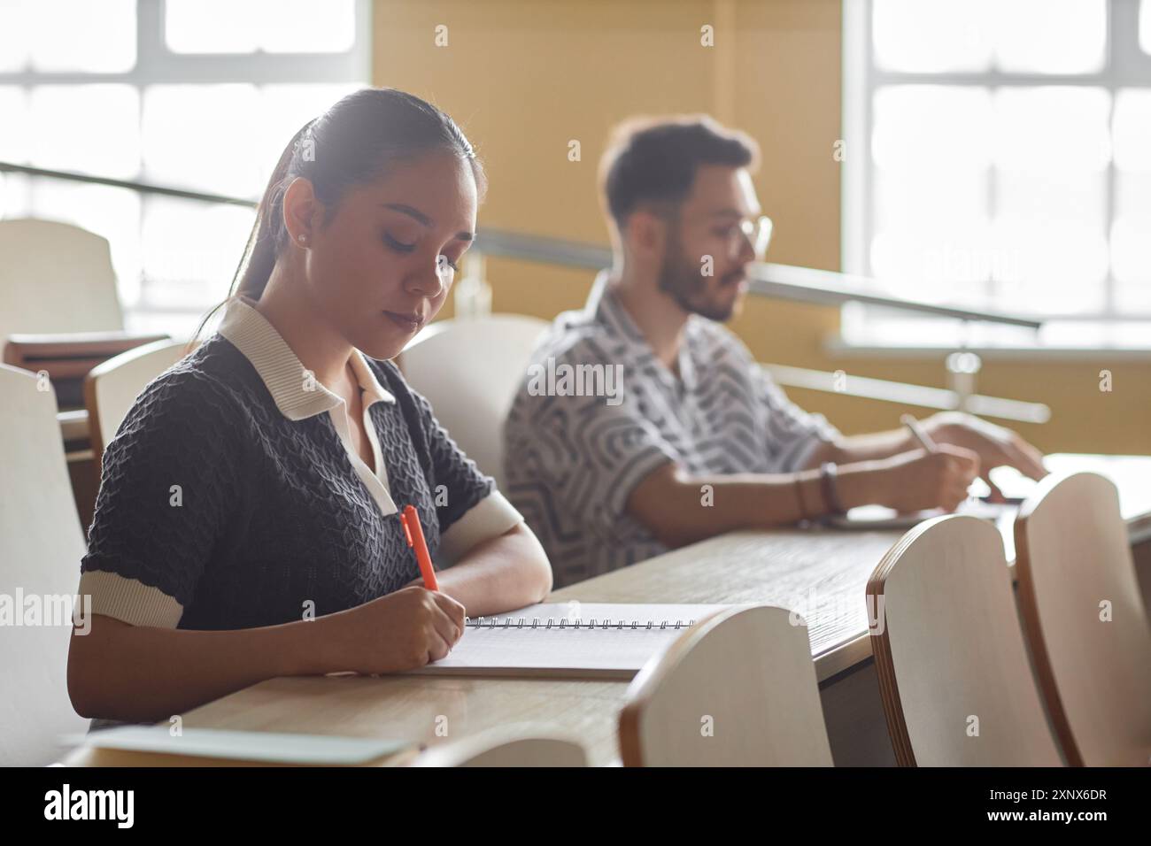 Side view of concentrated young Hispanic female student taking notes ...