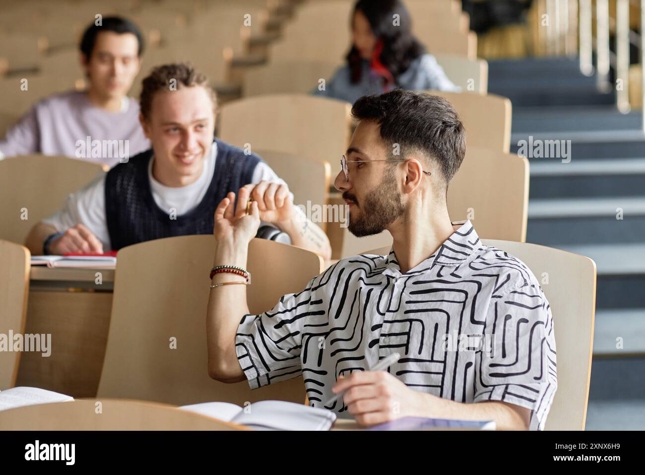 Side view shot of young male Middle Eastern student at desk secretly ...