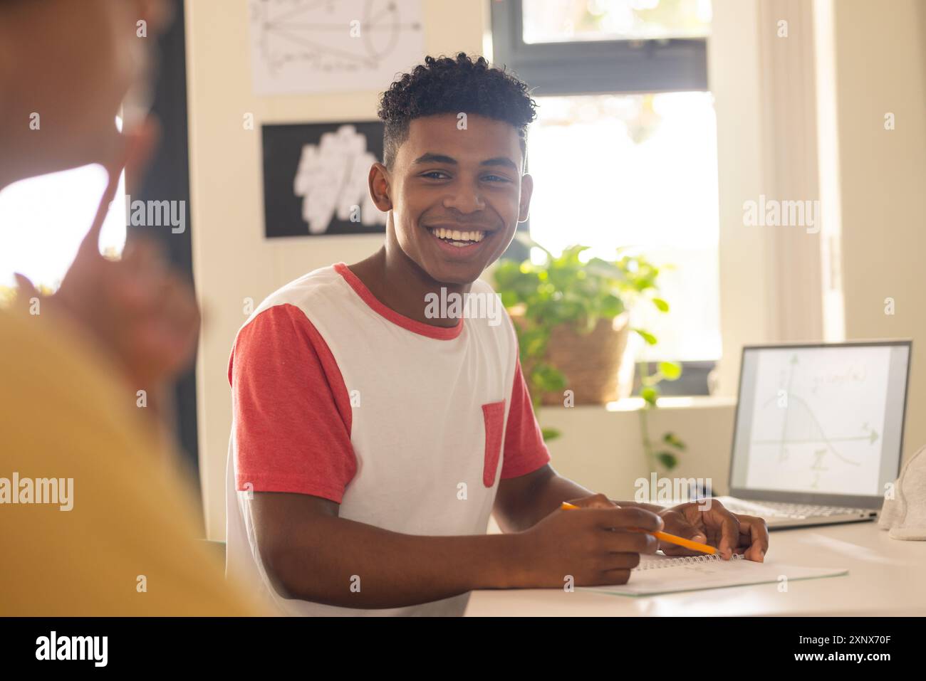 In high school, smiling teenage boy writing in notebook with laptop on ...