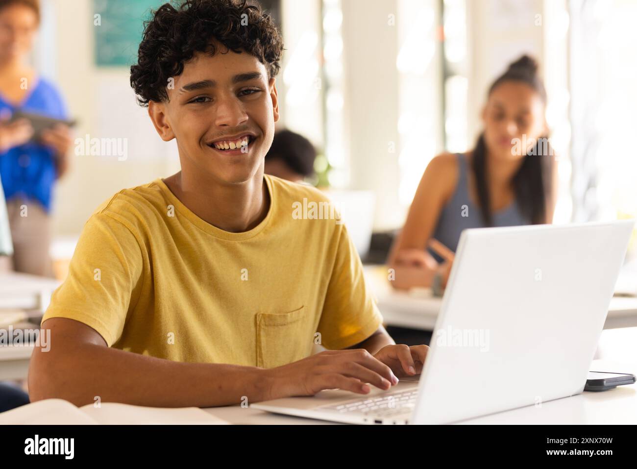 Smiling teenage boy using laptop in high school classroom, engaging in ...