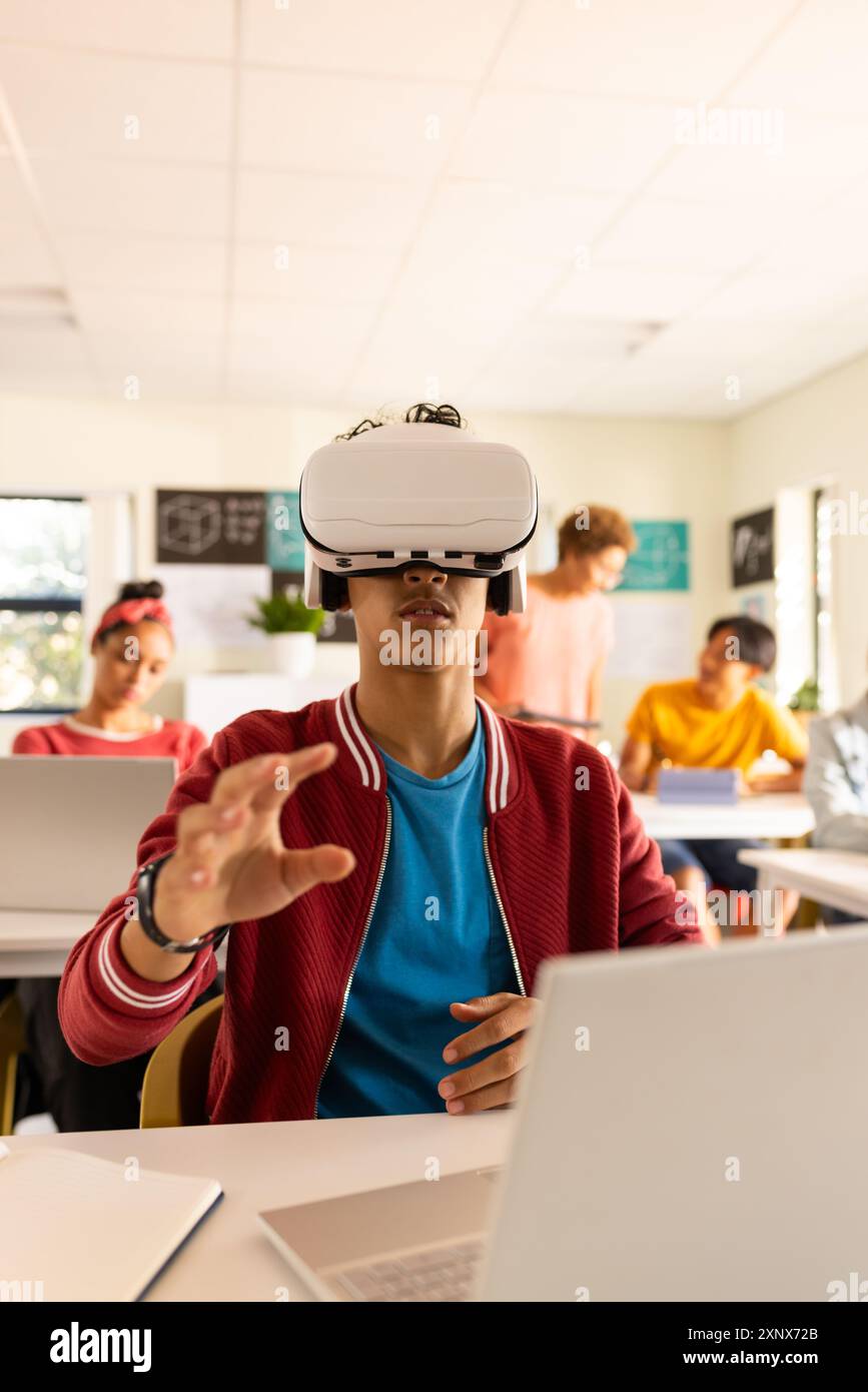 In high school, teenage boy using VR headset and laptop in classroom ...