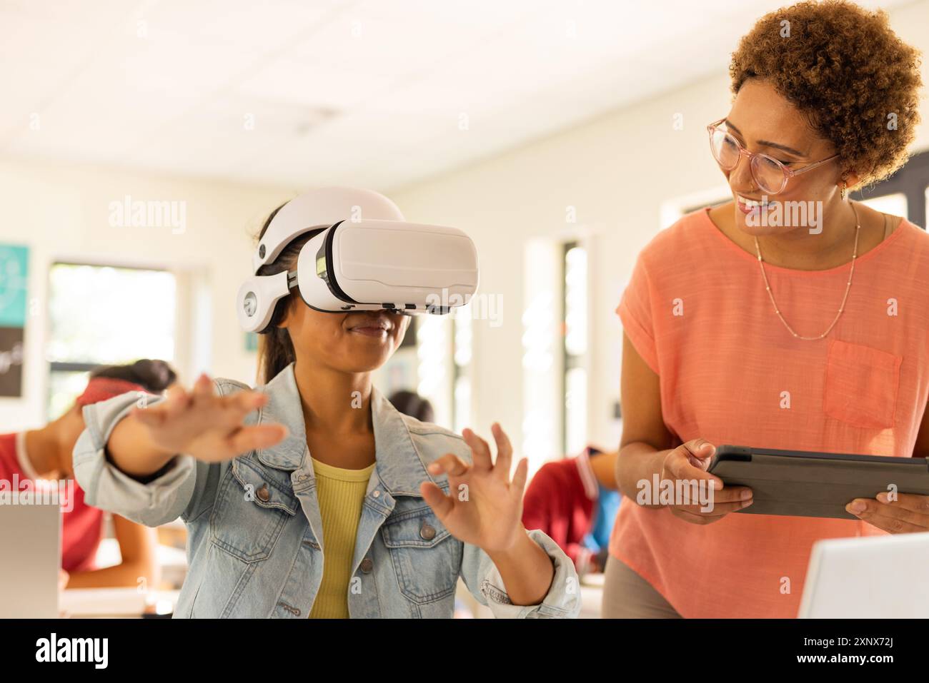 In high school, student using VR headset while teacher with tablet ...