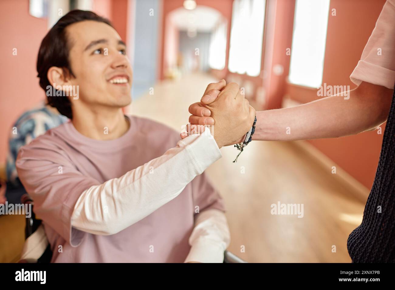HapYoung smiling male student in wheelchair giving male classmate ...