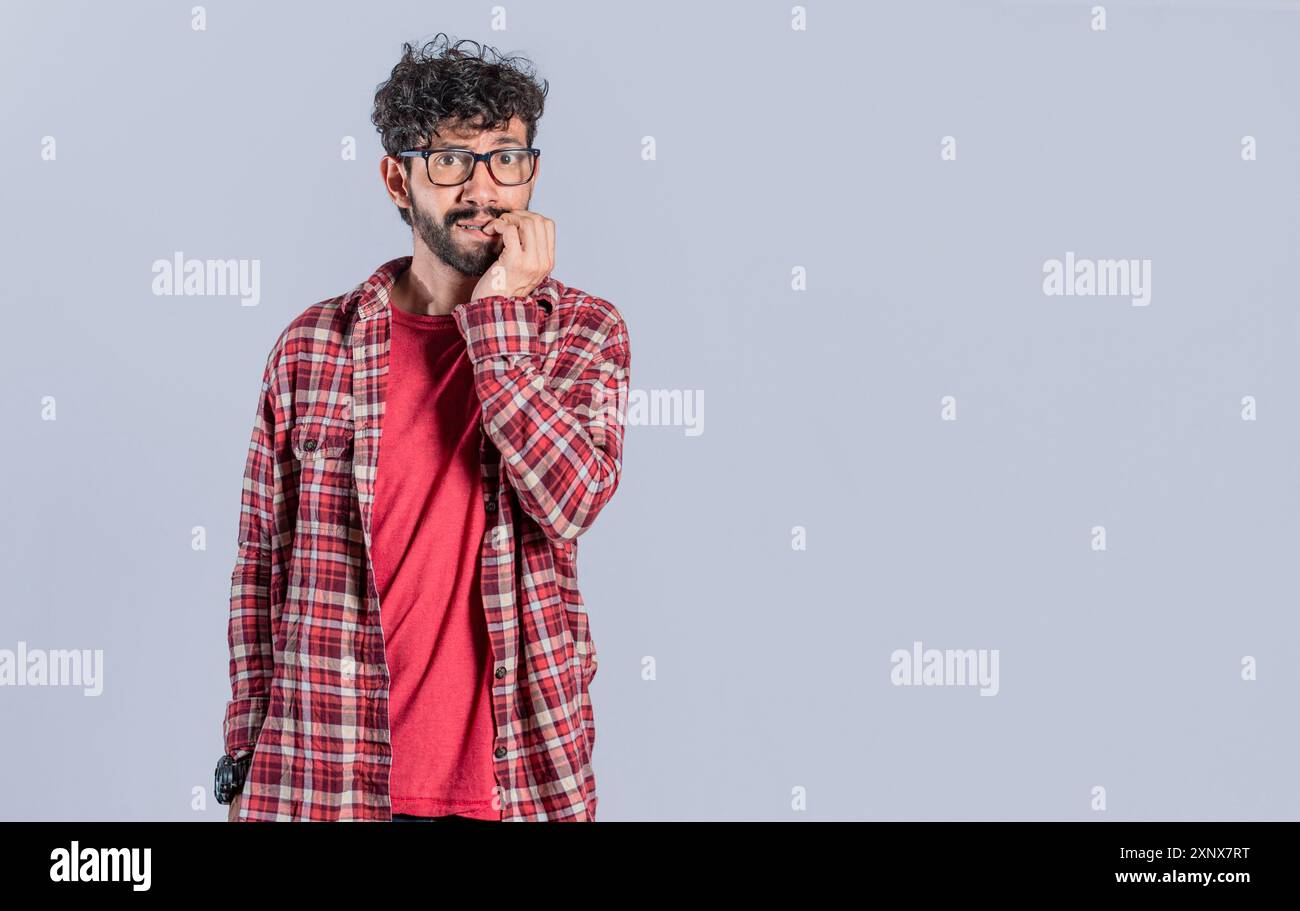 Nervous young man with worried expression bites nails and looks ...