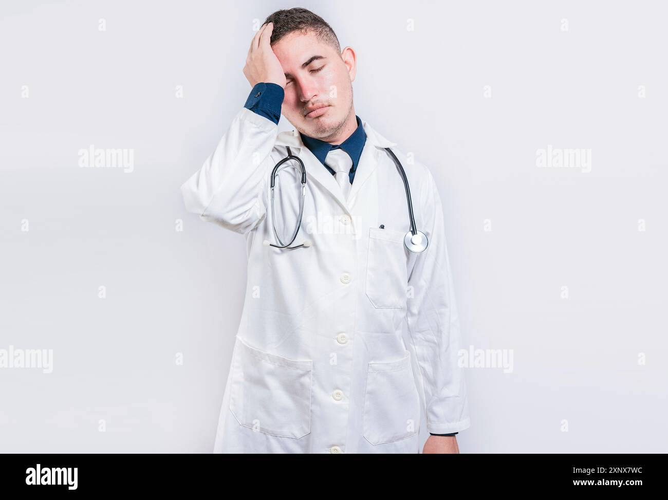 Exhausted young doctor with hand on forehead. Tired doctor with hand on ...