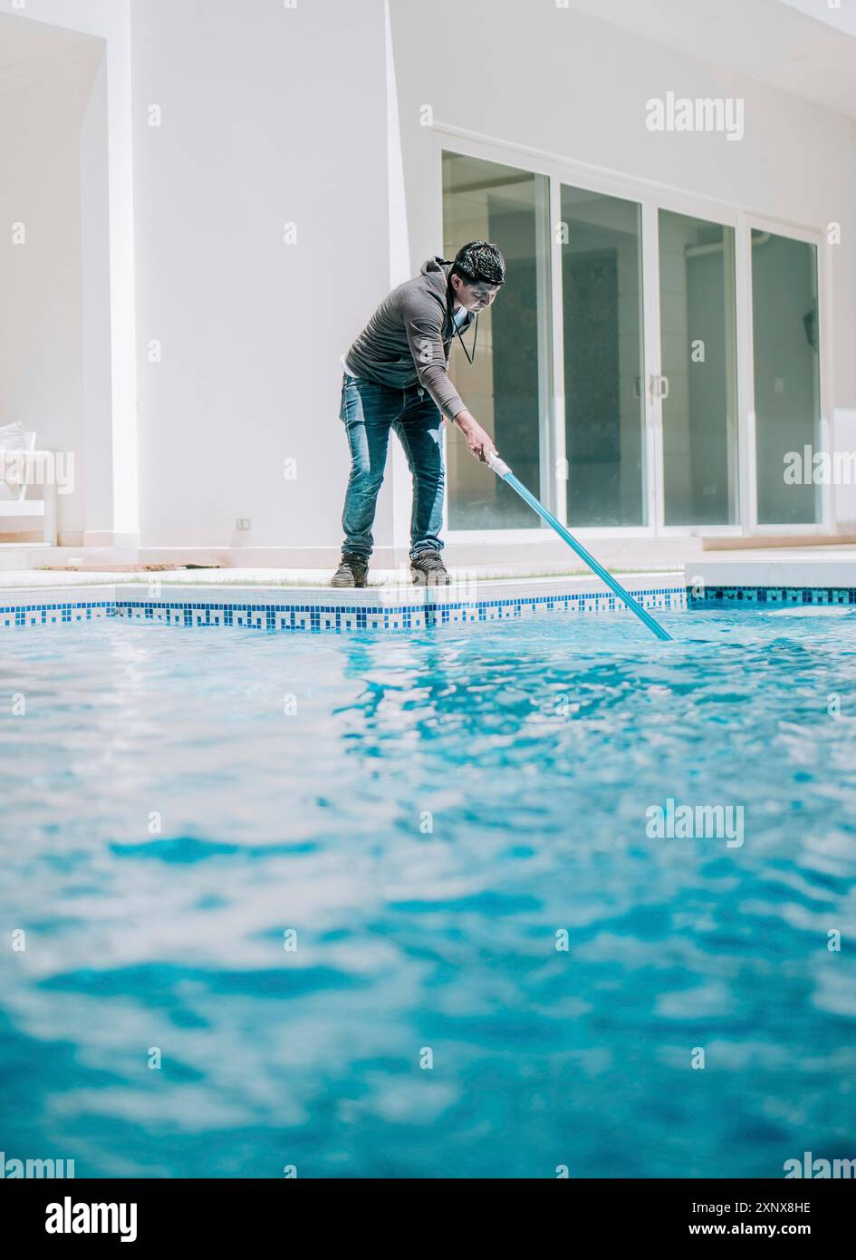 Young man cleaning a swimming pool with suction hose. Swimming pool ...