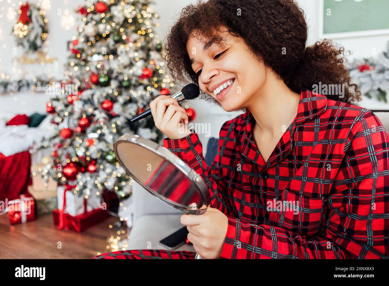 Cute African in pajamas looking in mirror and doing festive makeup ...