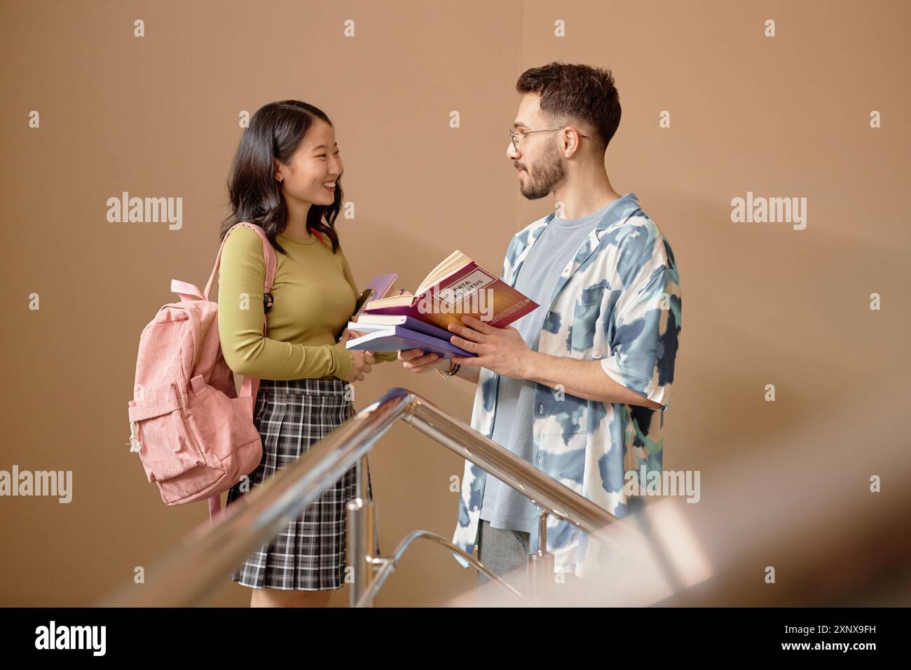 Side view of two multiethnic Gen Z student discussing coursebook in ...