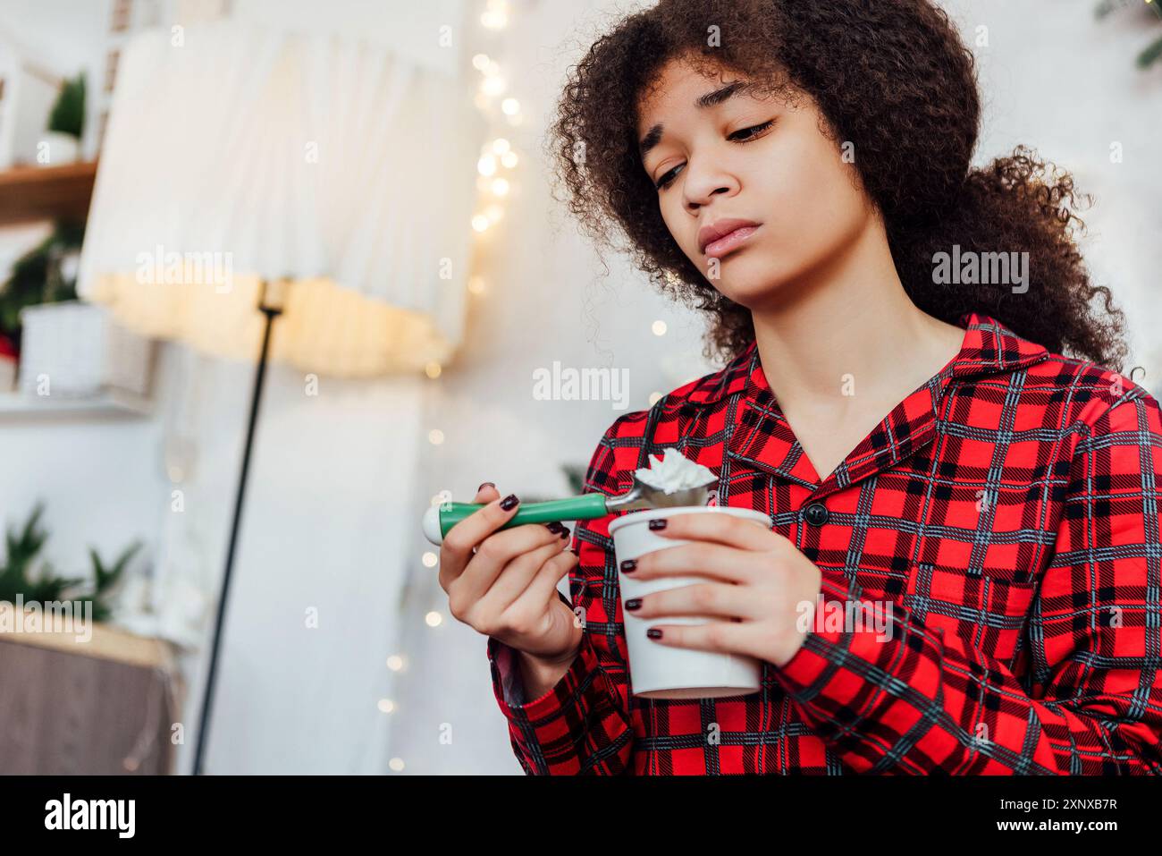 Young upset African woman in pajamas is sitting on bed and eating ...