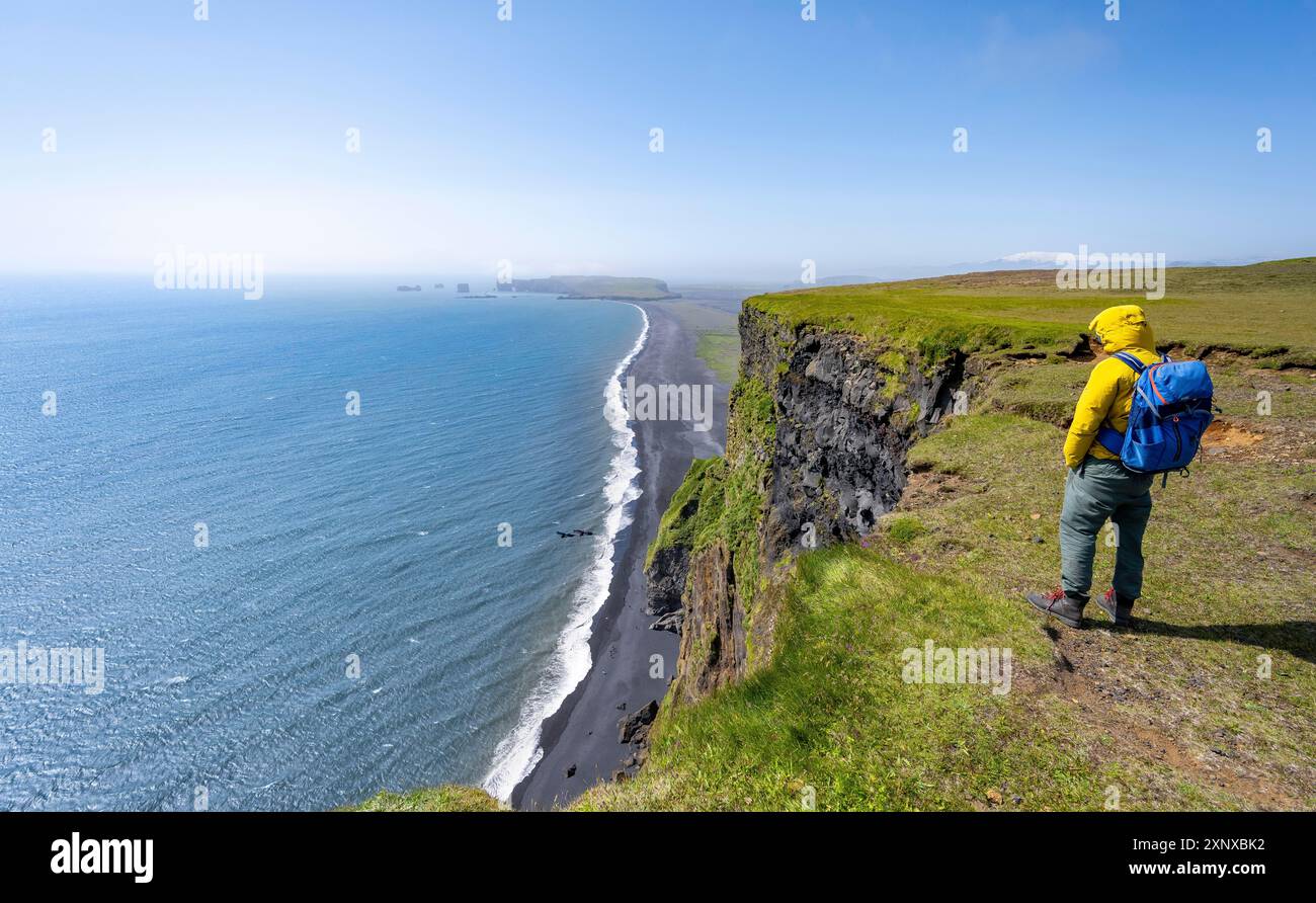Young man standing on cliff, view from steep cliff over Reynisfjara ...