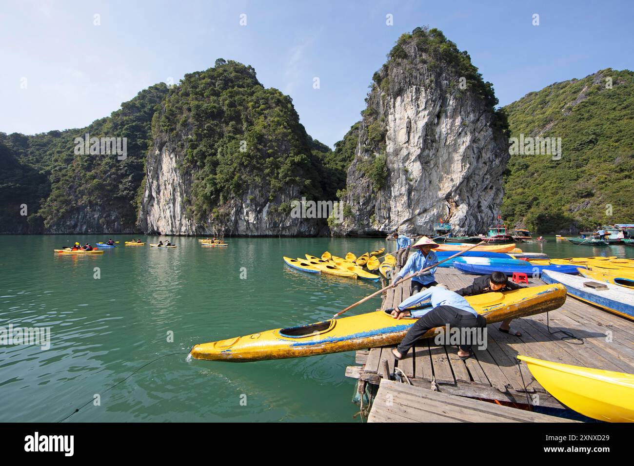 Vietnamese men pull a kayak onto a jetty, behind them the karst rocks ...