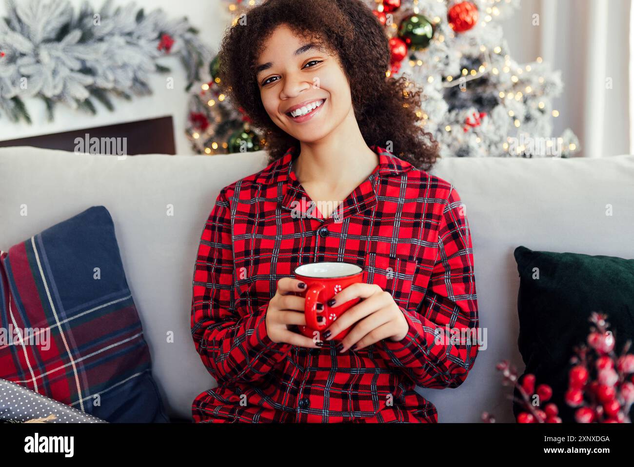 Cute African woman in pajamas sitting on couch and holding mug in ...