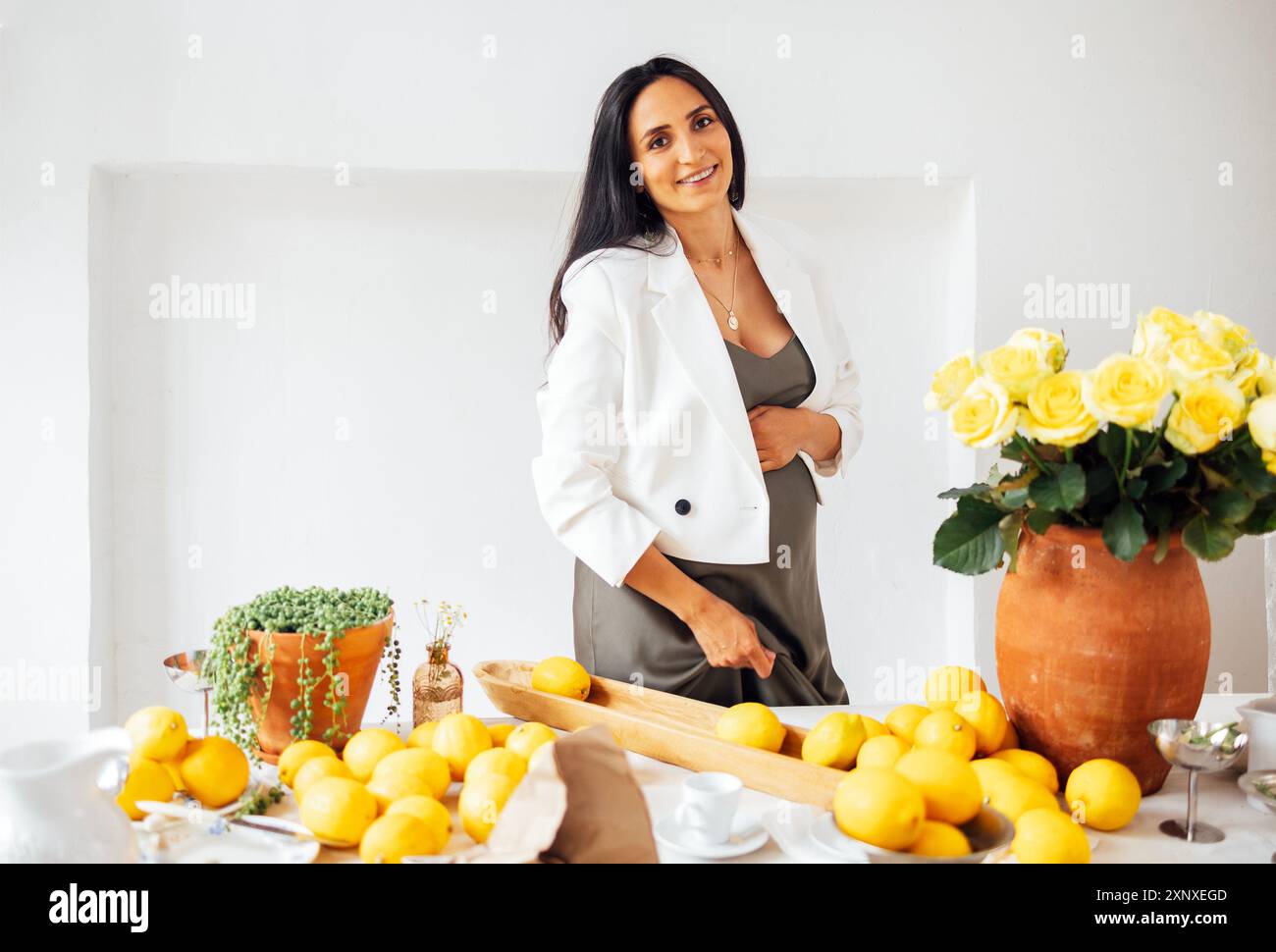 A young pregnant woman smiles and holds her belly in the kitchen ...