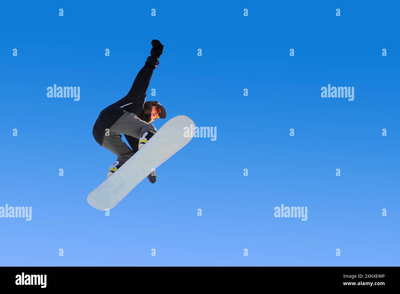 Snowboarder girl does a trick in jumping with a grab against the blue ...