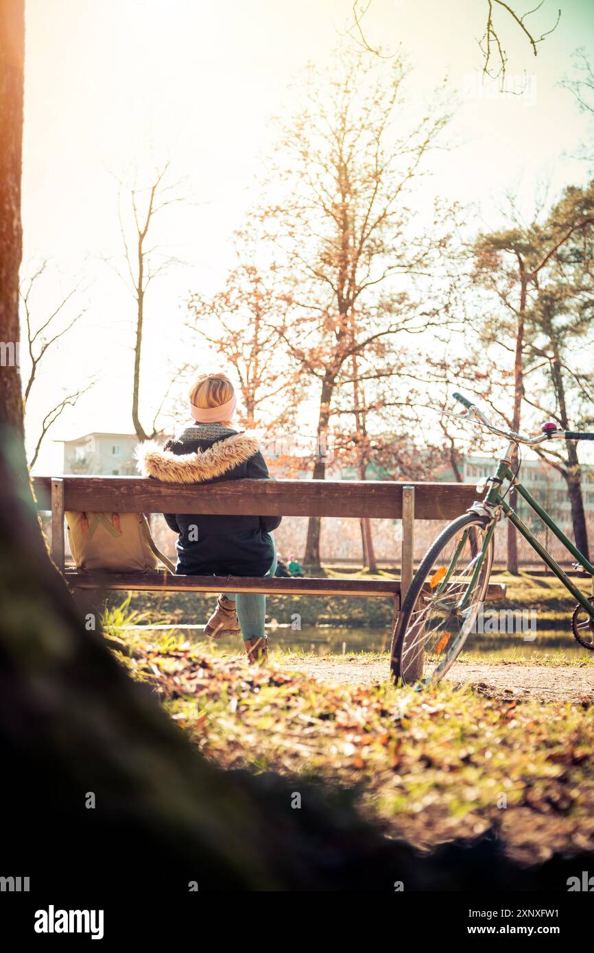 Back view of young woman with bicycle who is enjoying the sun on a park ...