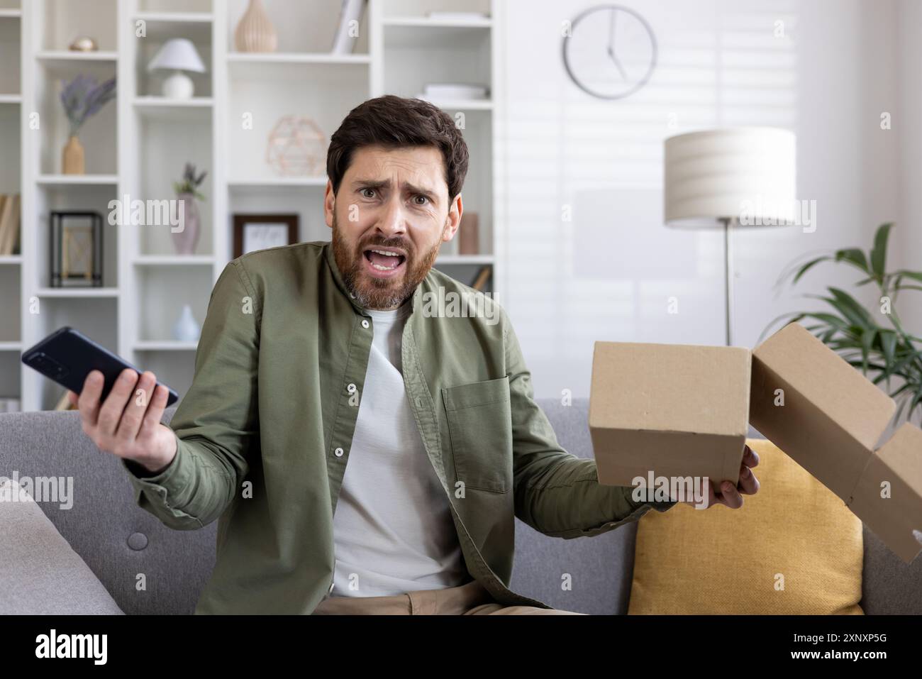 Frustrated man holding smartphone and open delivery box expressing ...