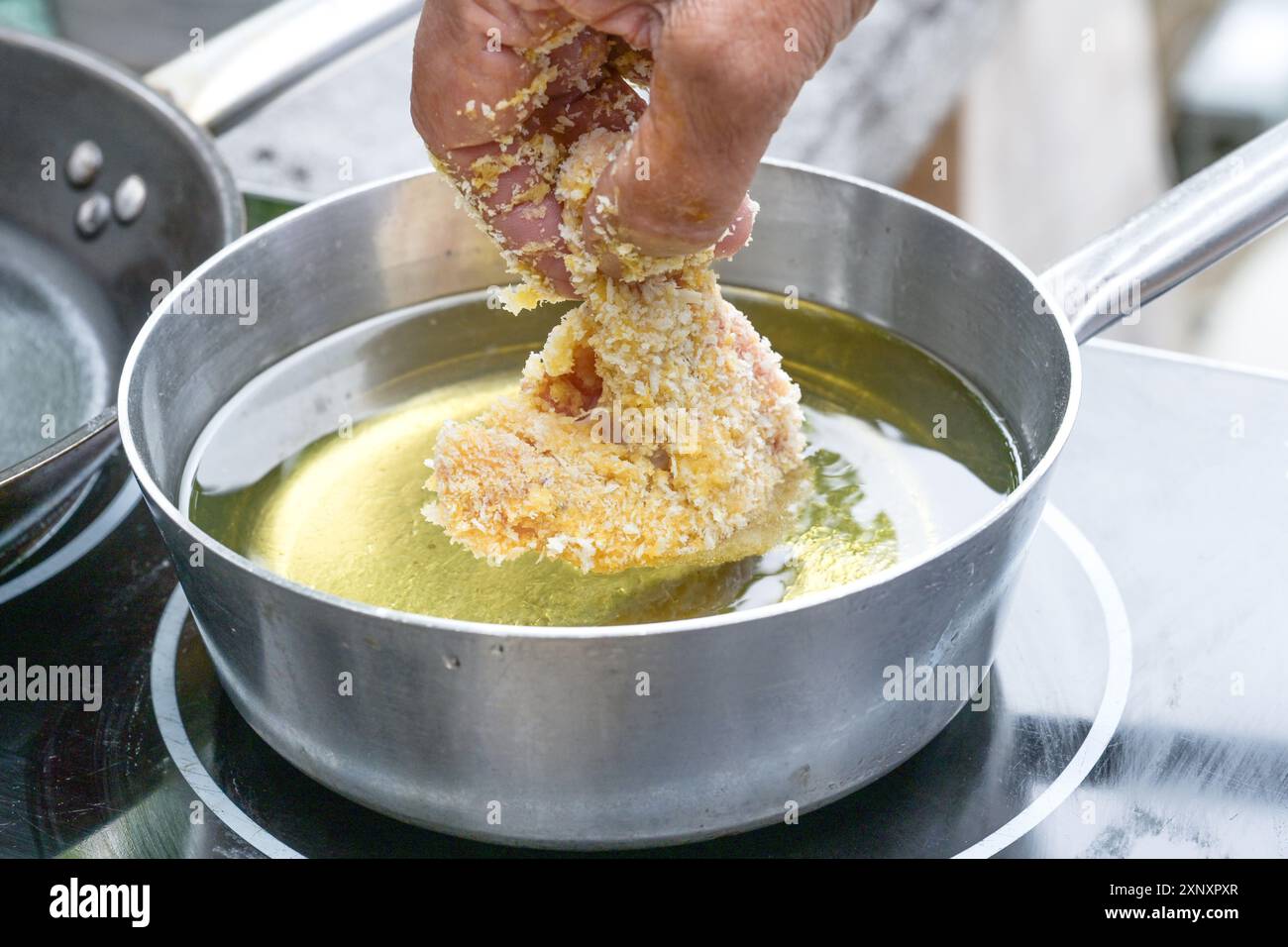 Hand carefully putting a piece of breaded chicken into a pot with ...