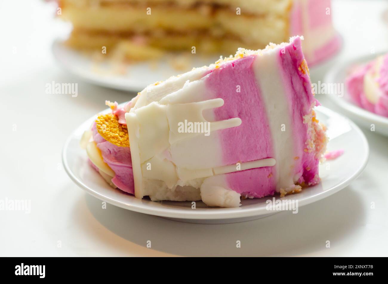 A slice of cake with pink frosting on a white plate. The cake is cut ...
