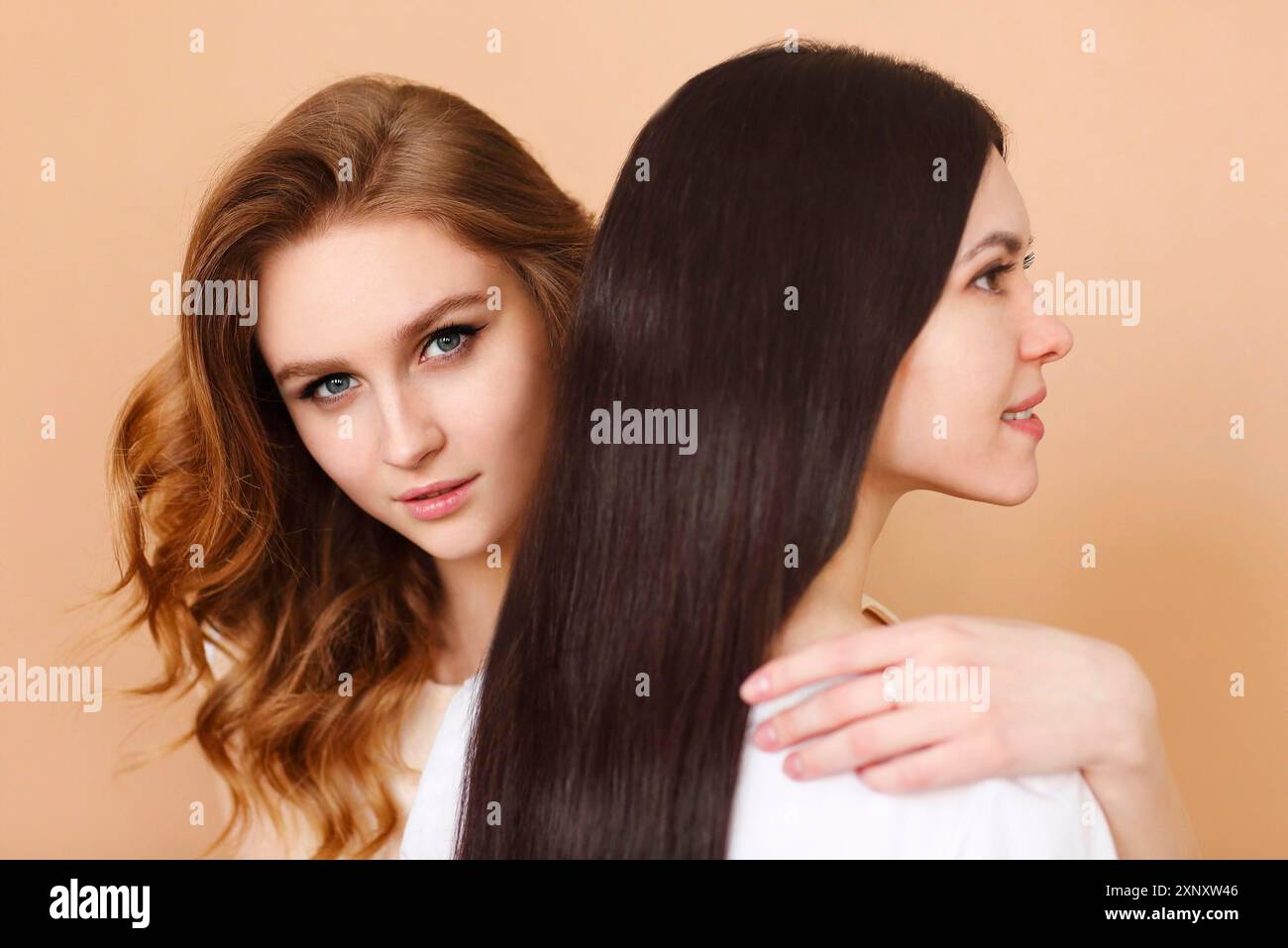 Two beautiful multicultural young women posing camera over beige ...