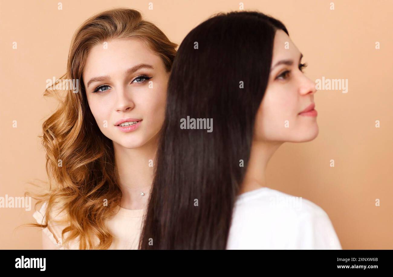 Two beautiful multicultural young women posing camera over beige ...