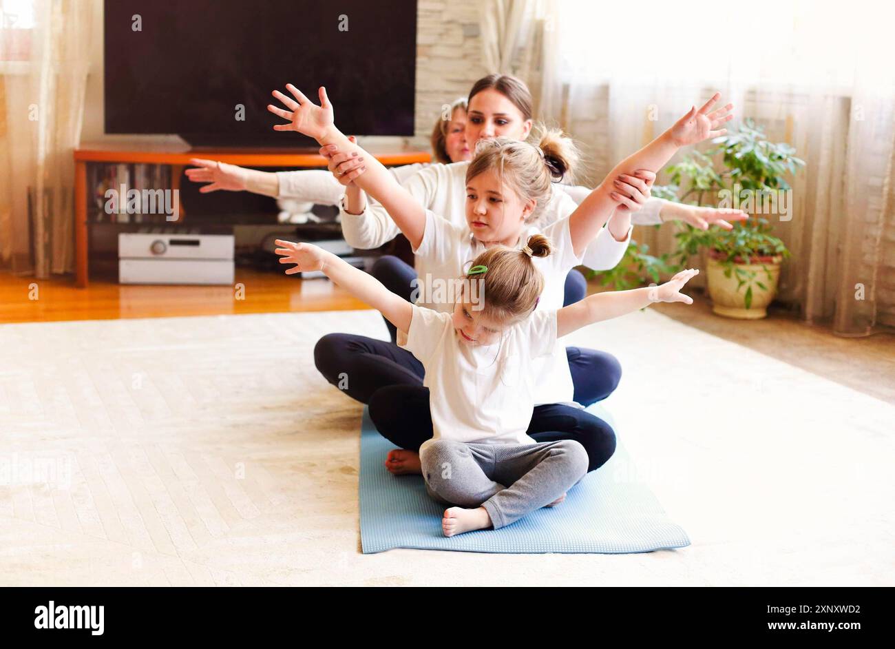 Adult women and little girls sitting in line on floor and stretching ...