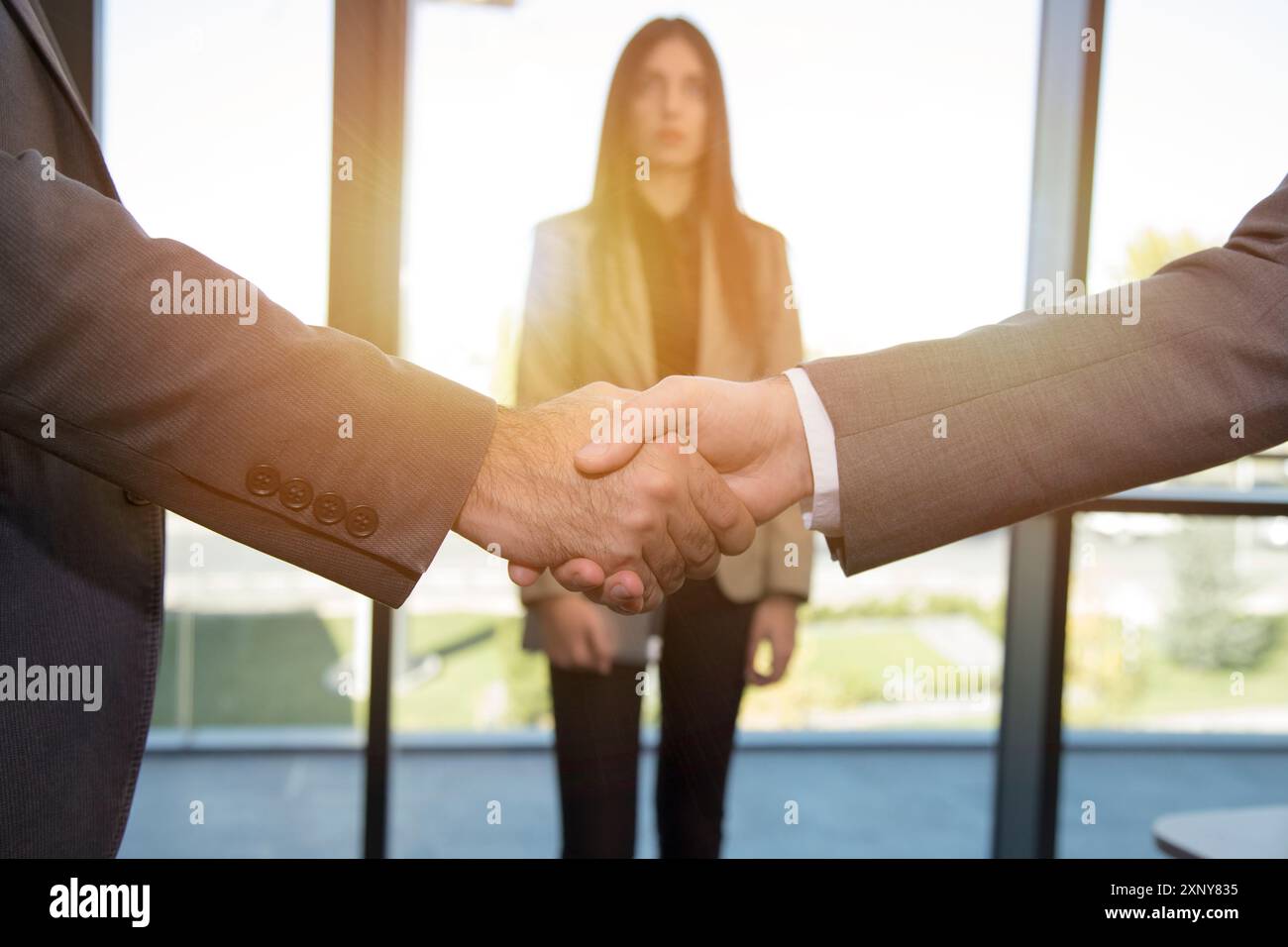 Two men shake hands in front of a woman Stock Photo - Alamy