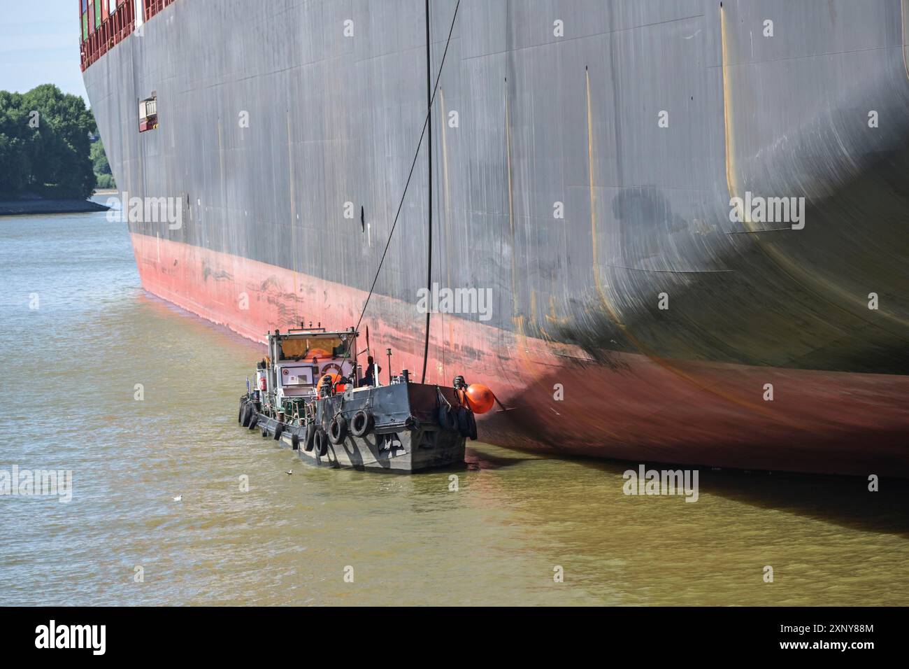Tanker boat or bunker barge at the hull of a large container freighter ...