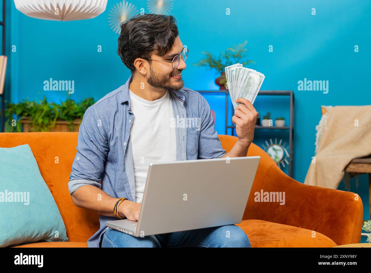 Planning budget. Rich happy Indian man counting money cash use laptop ...