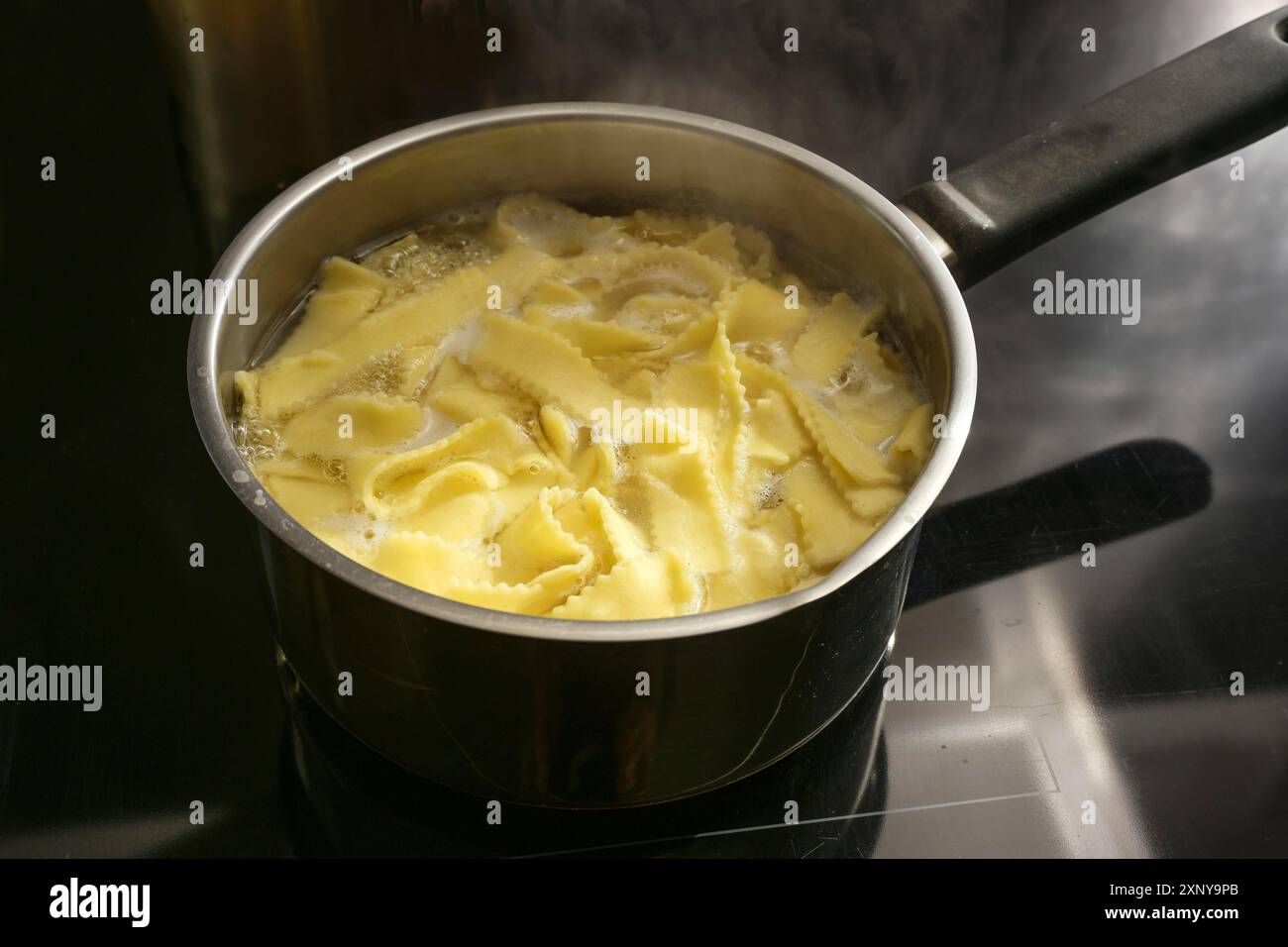 Pasta noodles are cooked in boiling water in a pot on a black stove top ...