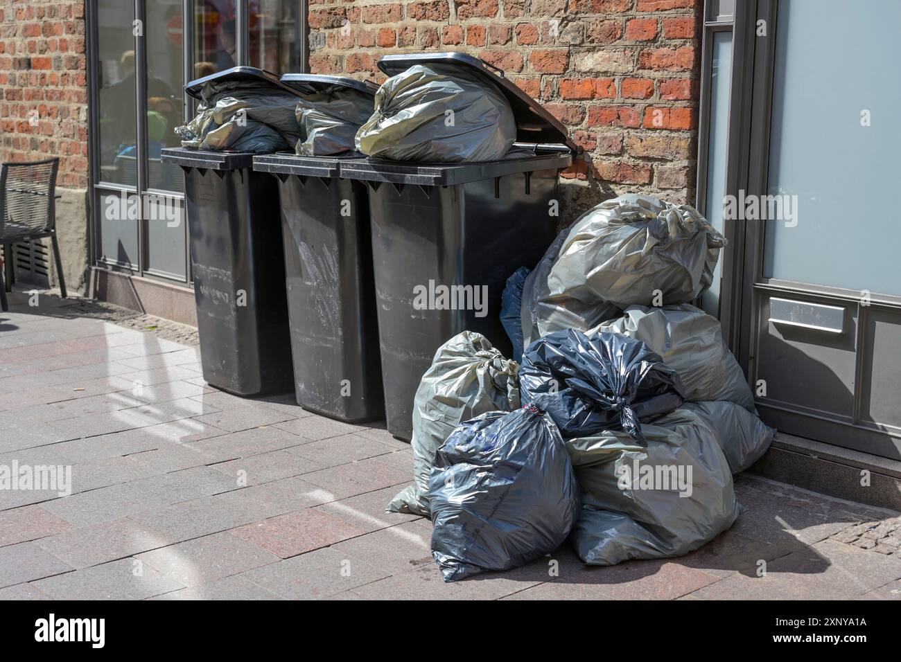 Overfilled trash bins and rubbish bags full of garbage on the pavement ...