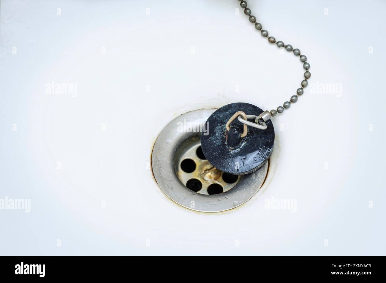 Old black rubber plug with metal chain on a rusty drain in a white wash ...