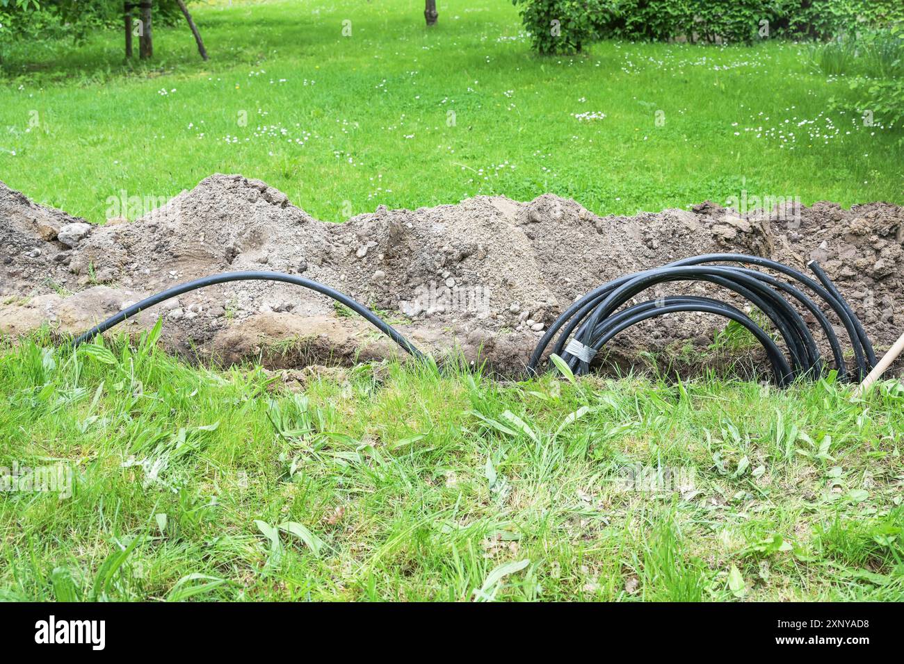Black power cable is laid in a narrow trench in the grass across the ...