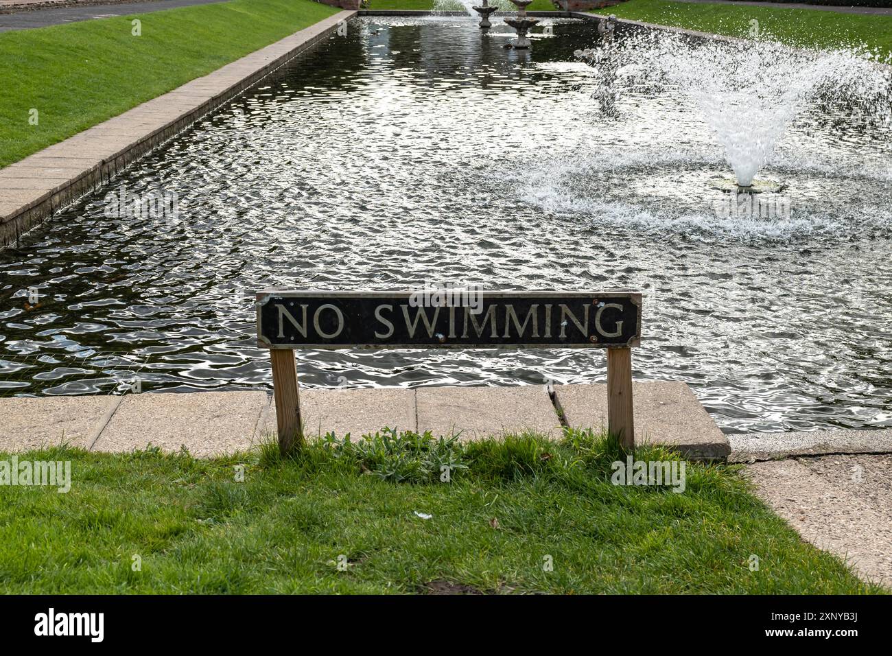 A 'NO SWIMMING' sign in front of a pond with a water fountain ...