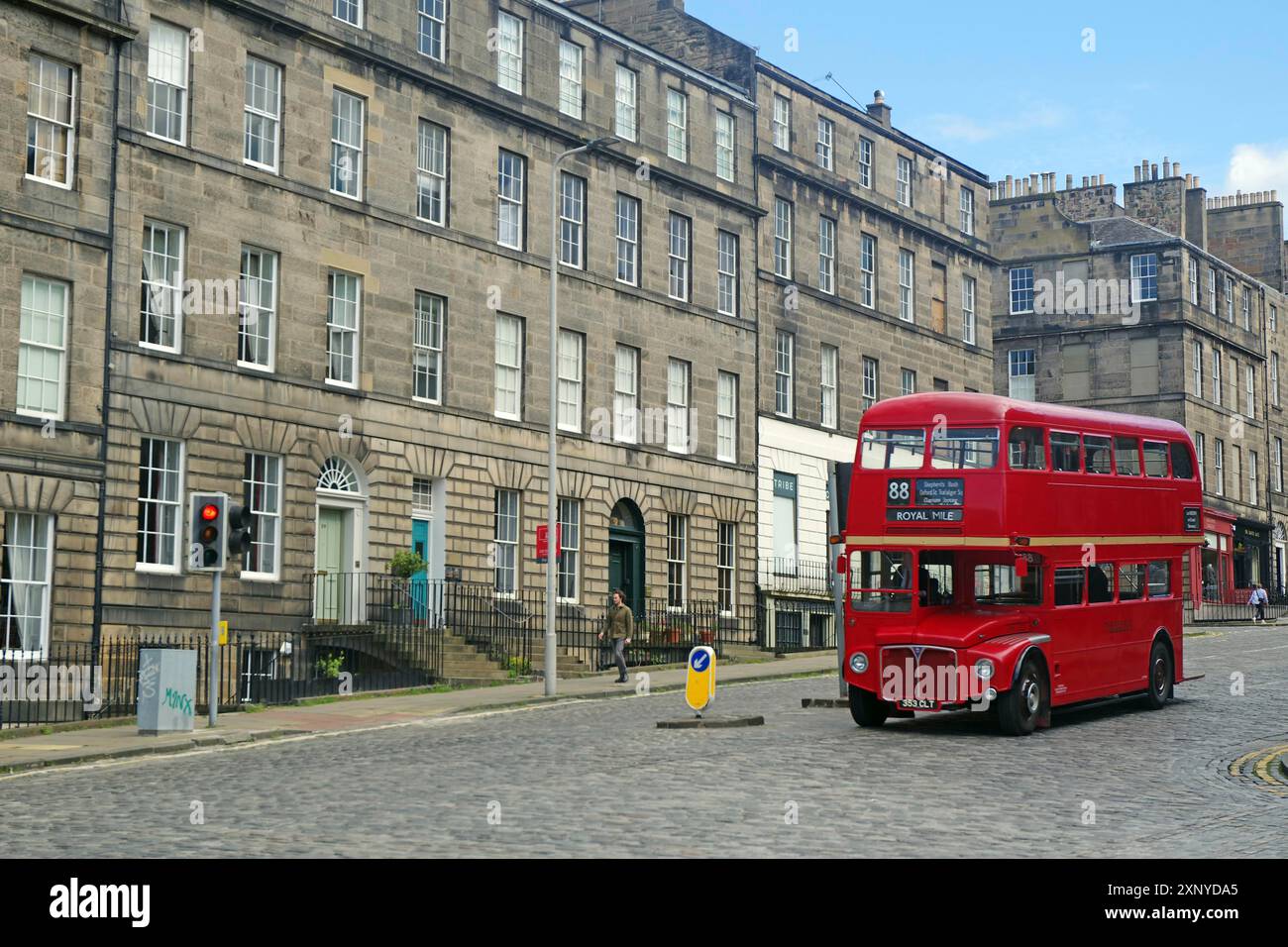 Red double-decker bus drives through a cobbled street in a historic ...