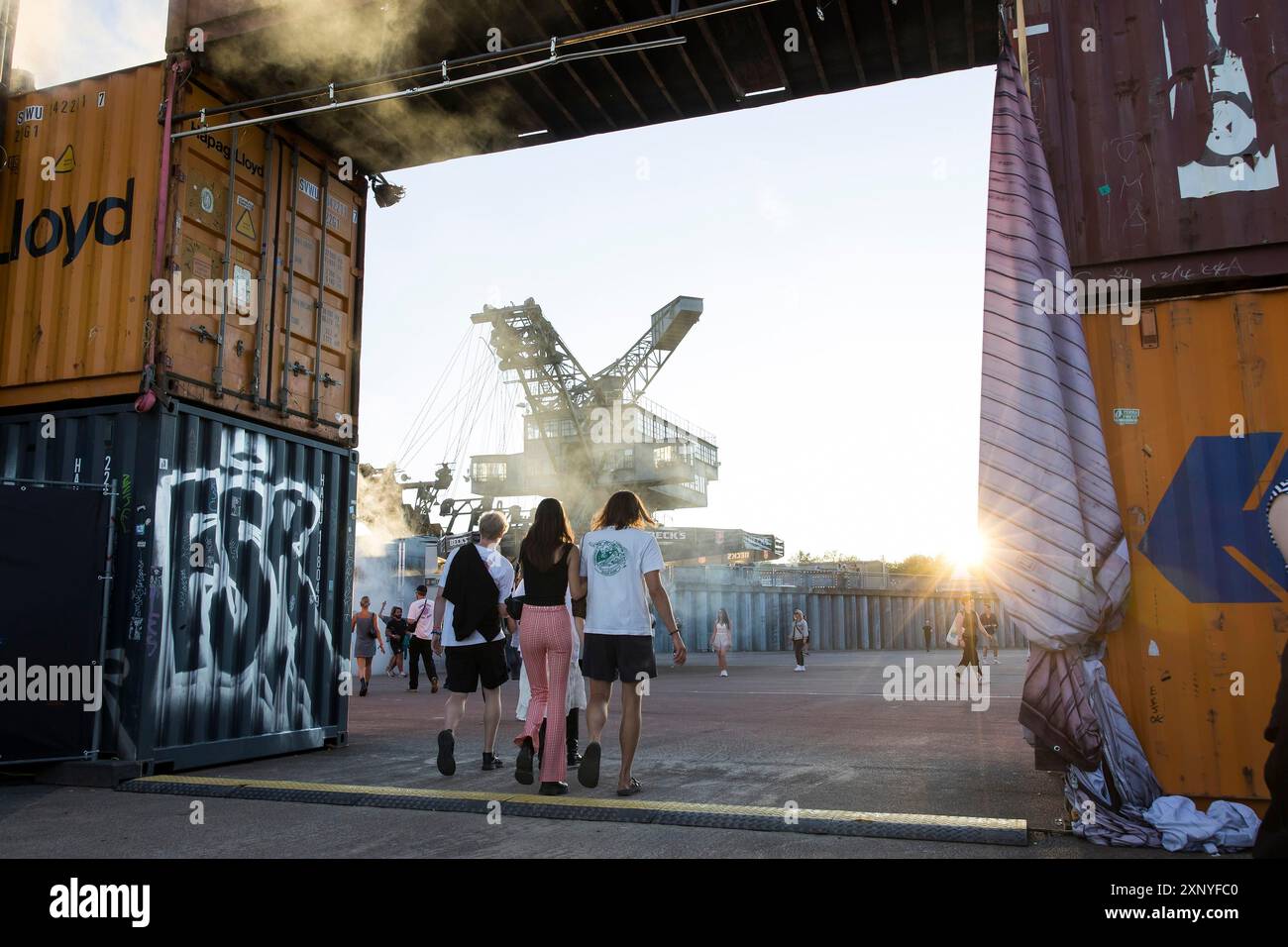 Festival visitors walk in the evening sun through a bridge made of ...