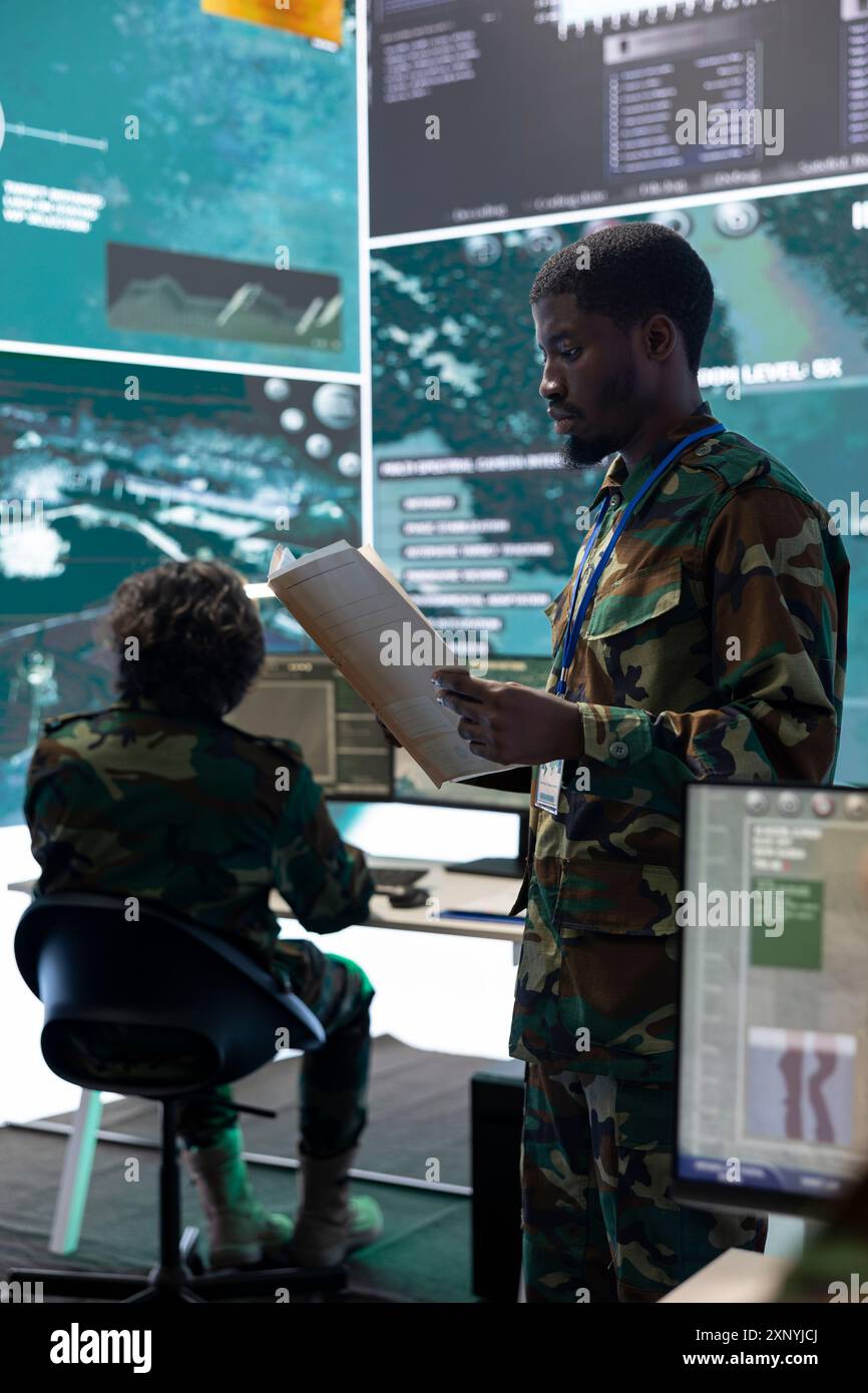 Army staff monitoring satellite surveillance activity on a big screen, troopers working in army ...