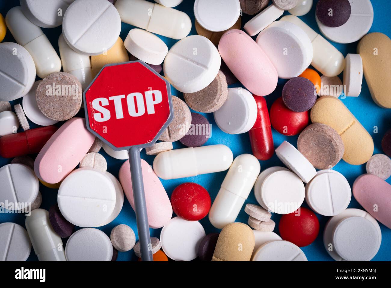 Red stop sign among different pills and capsules on blue background ...