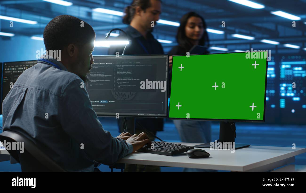 IT technician looking at green screen PC, working in data center, ensuring optimal performance ...